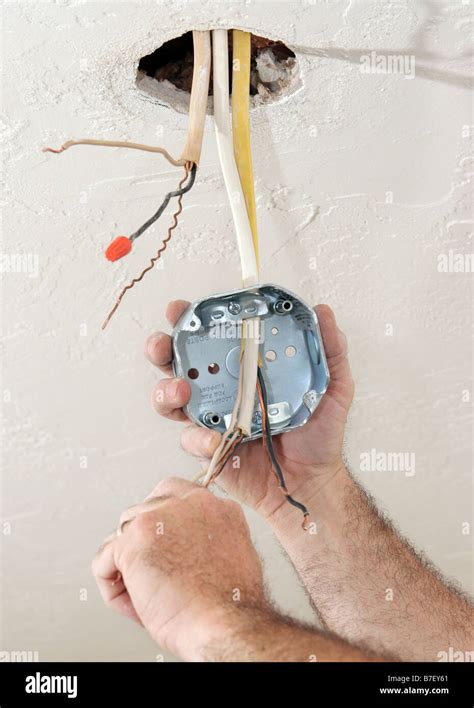 An Electrician Threading Wire Through A Regulation Fan Ceiling Box Work Being Performed To Code