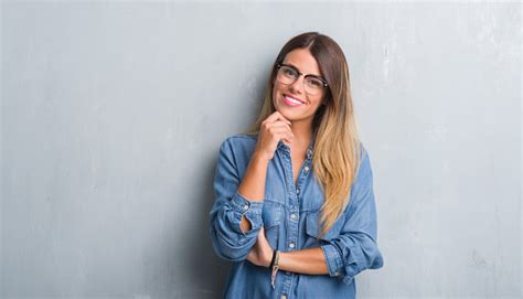 그런 지 위에 젊은 성인 여자 회색 벽 턱 질문 잠겨있는 표현에 대 한 생각에 손으로 안경을 사려깊은 얼굴 미소 의심 개념입니다