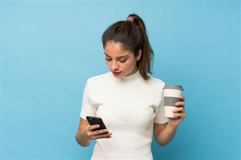 Jovem Menina Morena Isolado Azul Segurando Caf Para Levar E Um Celular Foto Premium