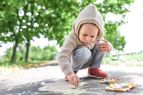 어린 소년 45 세 후드와 따뜻한 스웨터에 포장에 크레용으로 그립니다 창조적 인 그림을 만듭니다 가을 공원에서 여름에 배경 녹색 나무와 단풍 Theatrical