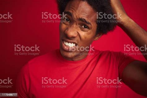 고립된 빨간 배경 위에 서있는 티셔츠를 입은 젊은 미국 남자는 머리에 손으로 스트레스를 받고 수치심과 깜짝 얼굴에 충격을 받았으며 화가 나고 좌절했습니다 실수에 대한