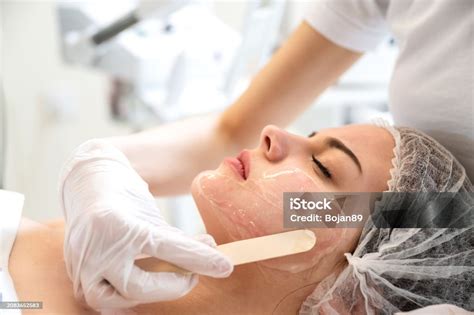 아름다운 젊은 여성의 얼굴에 화장품 젤 필링 마스크를 적용하는 나무 주걱으로 미용사 손의 근접 촬영 껍질에 대한 스톡 사진 및