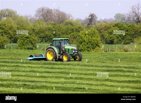 John Deere Tractor Using A Roller To Flatten Grass On A Field Stock