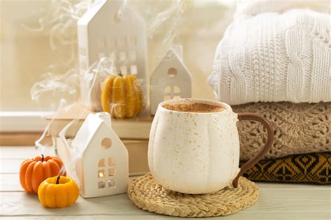 가을 작곡 뜨거운 커피 한 잔 장식용 작은 집 호박 양초 책 나무 테이블에 따뜻한 스웨터 계절에 따라 따뜻한 아침 커피 아늑한