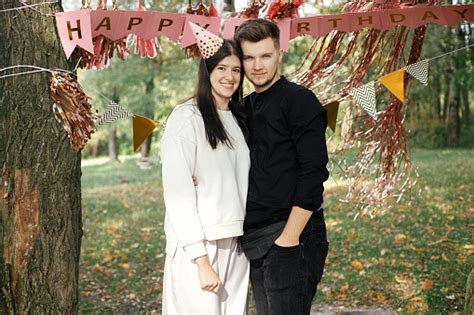 파티에서 행복한 여자와 공원에서 분홍색 생일 화환의 배경에 껴안고 잘 생긴 남자 야외 피크닉 파티에서 가족 및 친구들과 생일을 축하하는 젊은 세련된 커플 2명에 대한 스톡