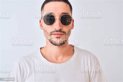 선글라스와 캐주얼 티셔츠를 입은 젊은 잘생긴 남자는 심각한 생각 스마트 얼굴에 자신감 표정으로 고립 된 배경 위에 T 셔츠에